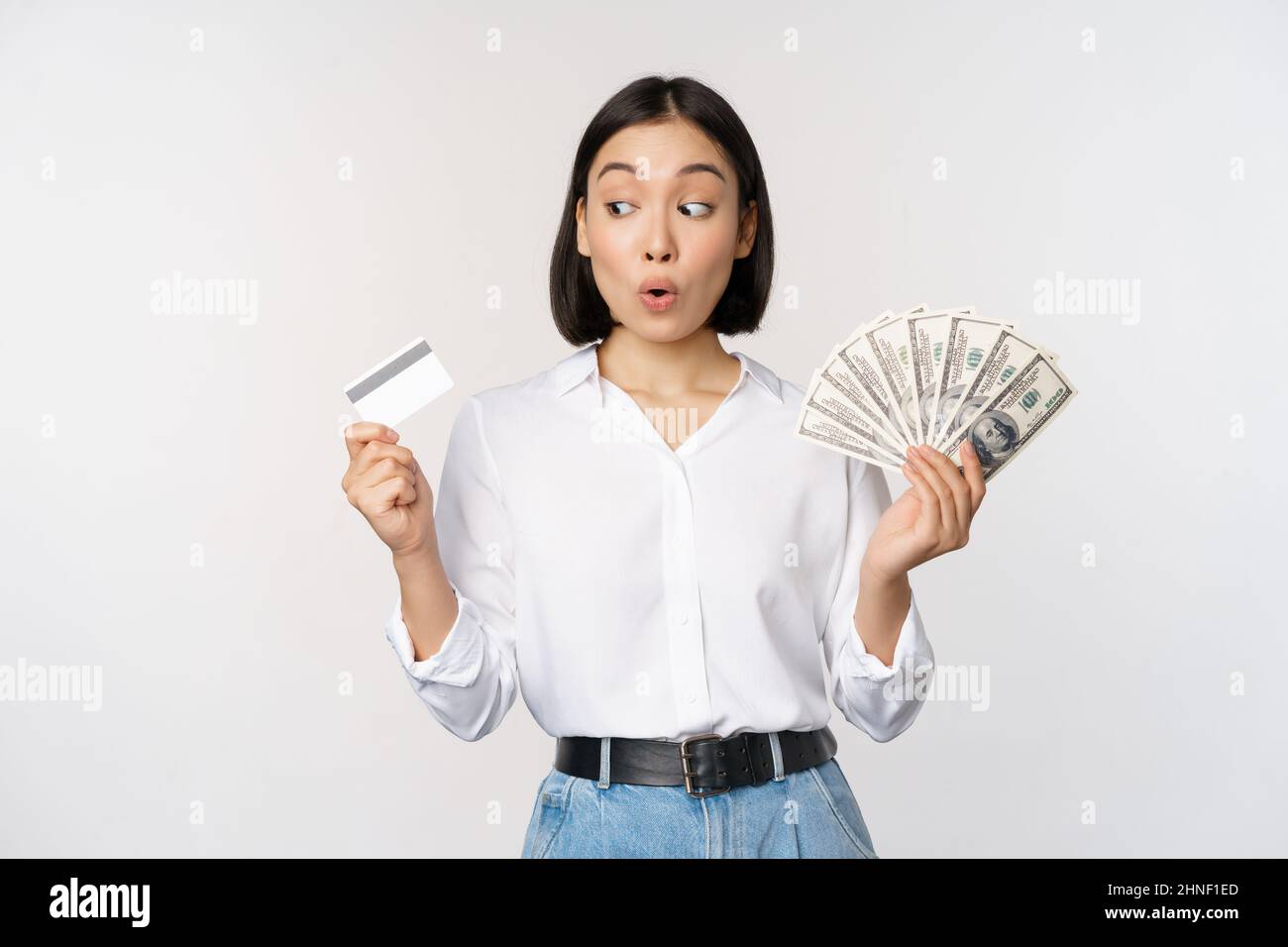 Excited korean girl looking at credit card, holding money cash, posing ...