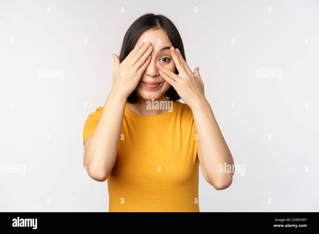 Cute korean female model, cover eyes with hands, peeking through fingers curious, watching smth ...