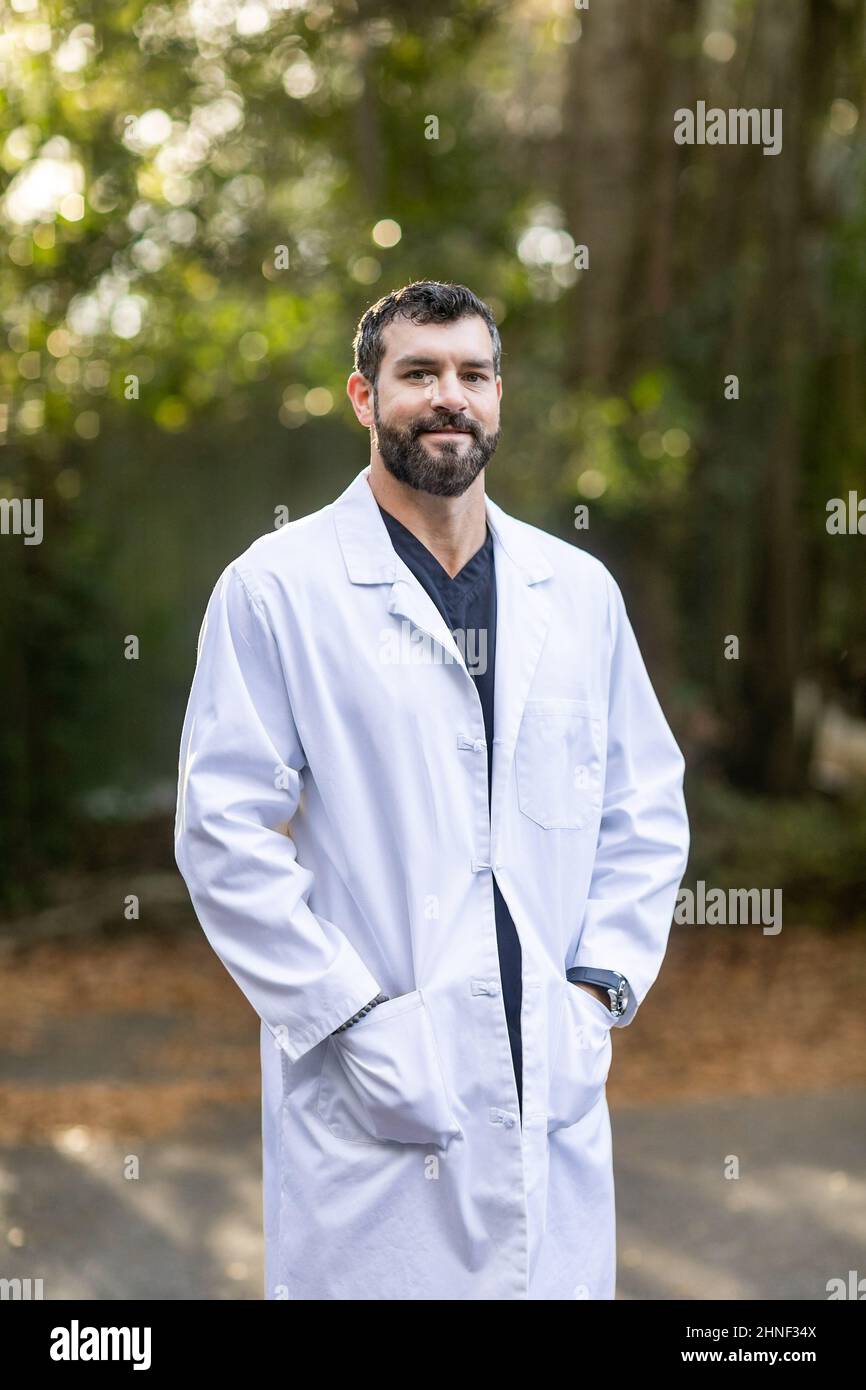 A doctor with dark hair and a beard in a white lab coat standing ...