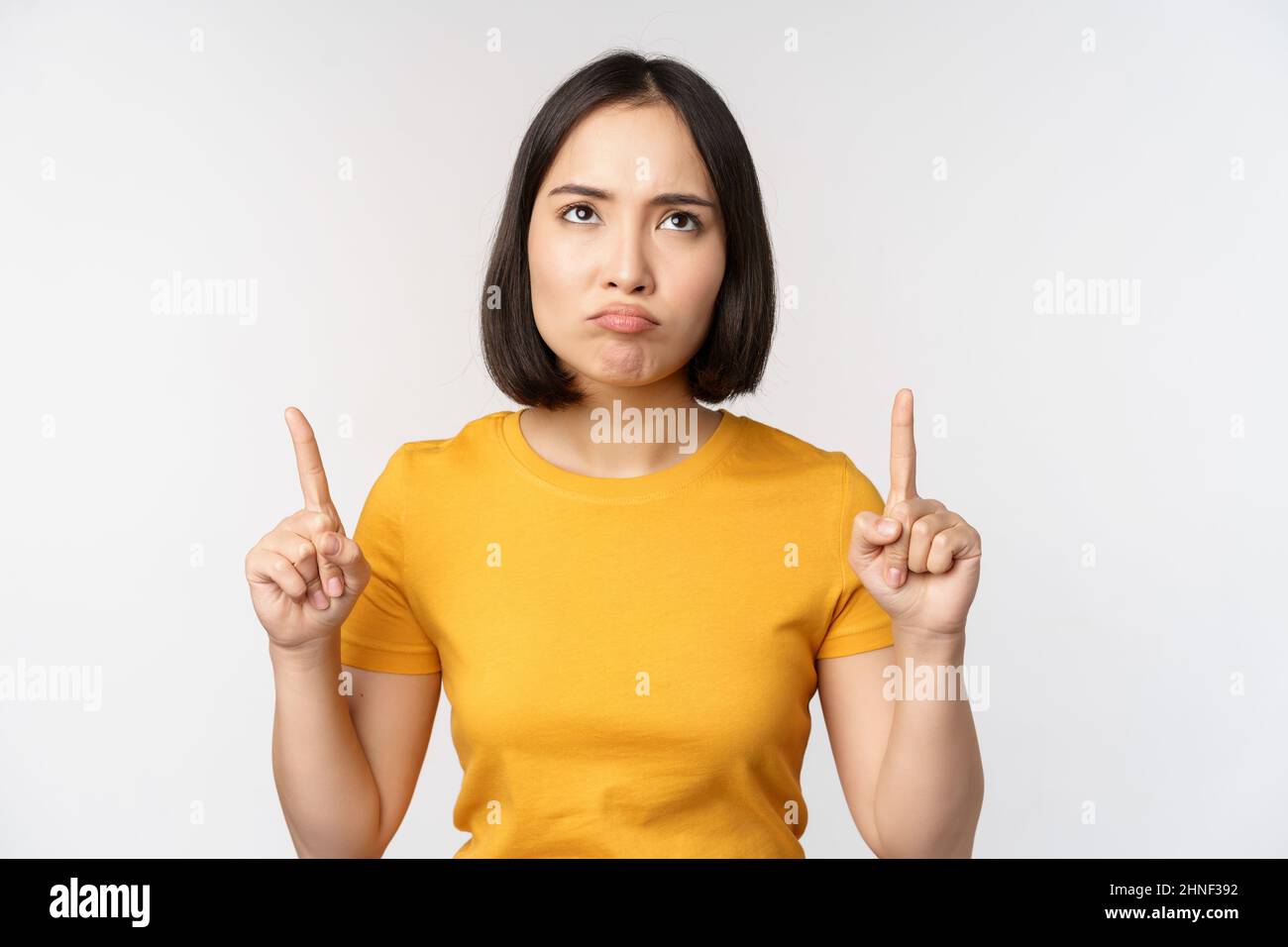 Disappointed asian woman looking, pointing fingers up with angry moody ...