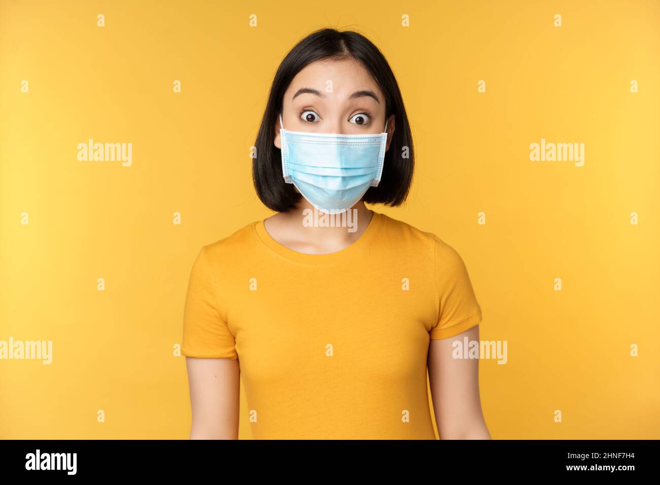 Portrait of korean girl in medical face mask looking surprised, amazed ...