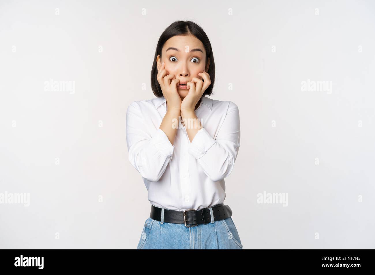 Portrait of scared asian woman watching smth scary, biting fingers on ...