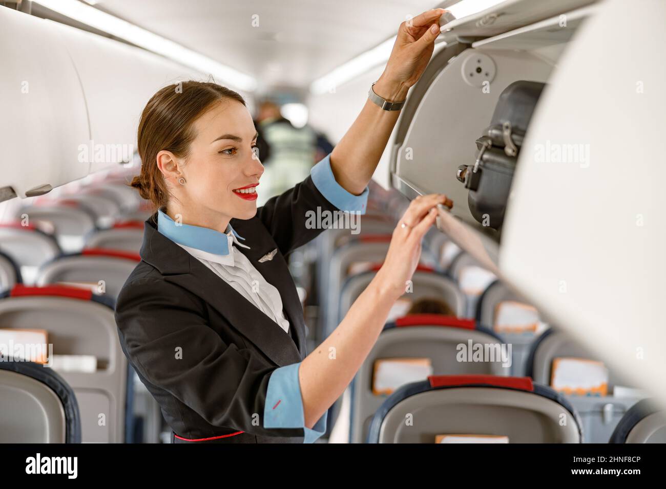 Joyful stewardess checking overhead luggage bin in airplane Stock Photo ...