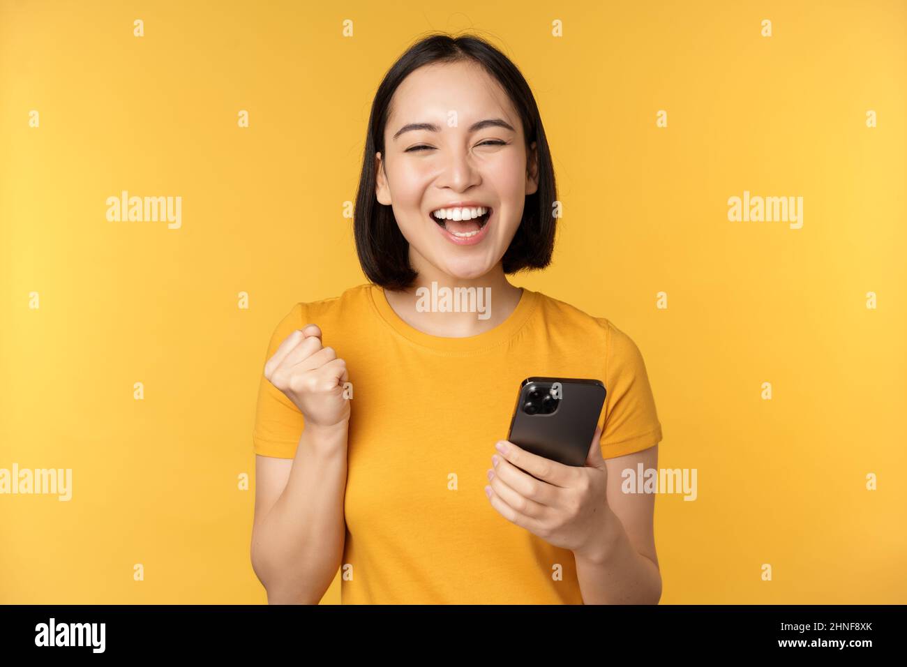 Joyful asian woman celebrating, holding mobile phone, winning, achieve ...