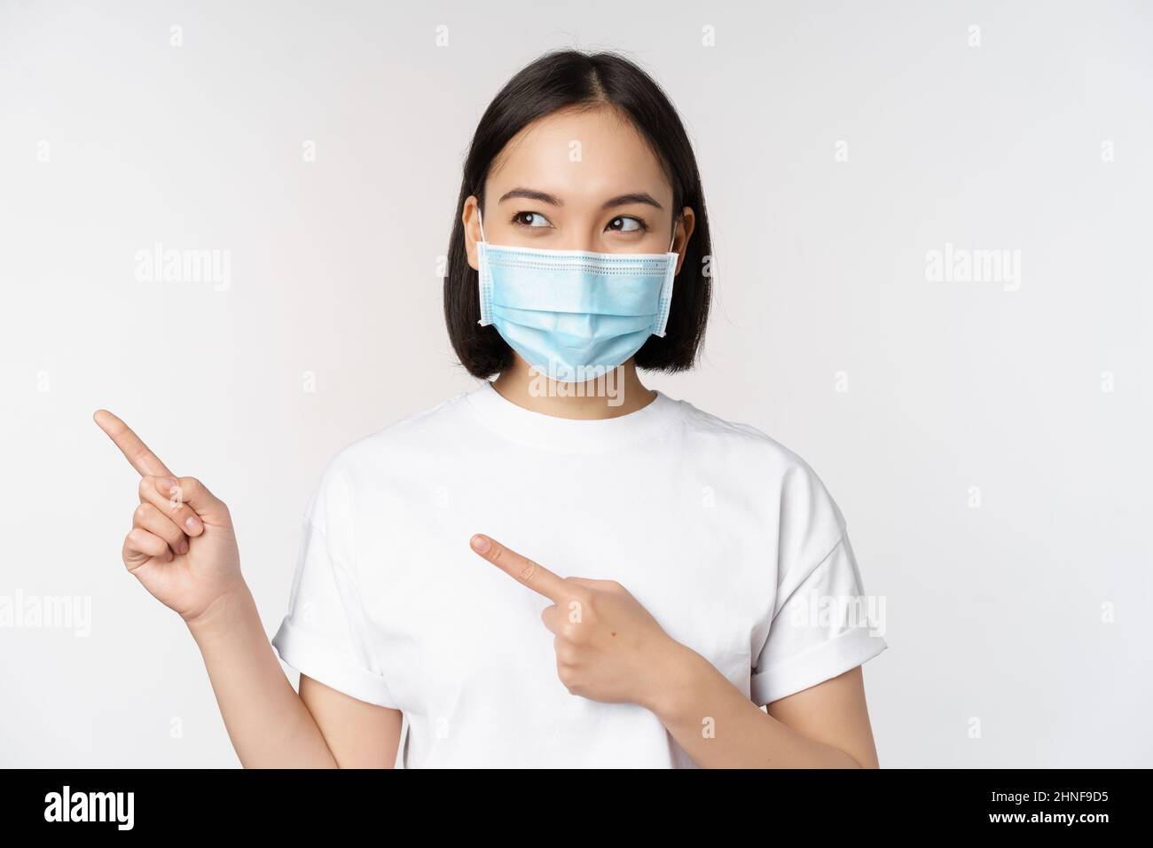 Young korean woman in medical face mask pointing fingers left and ...