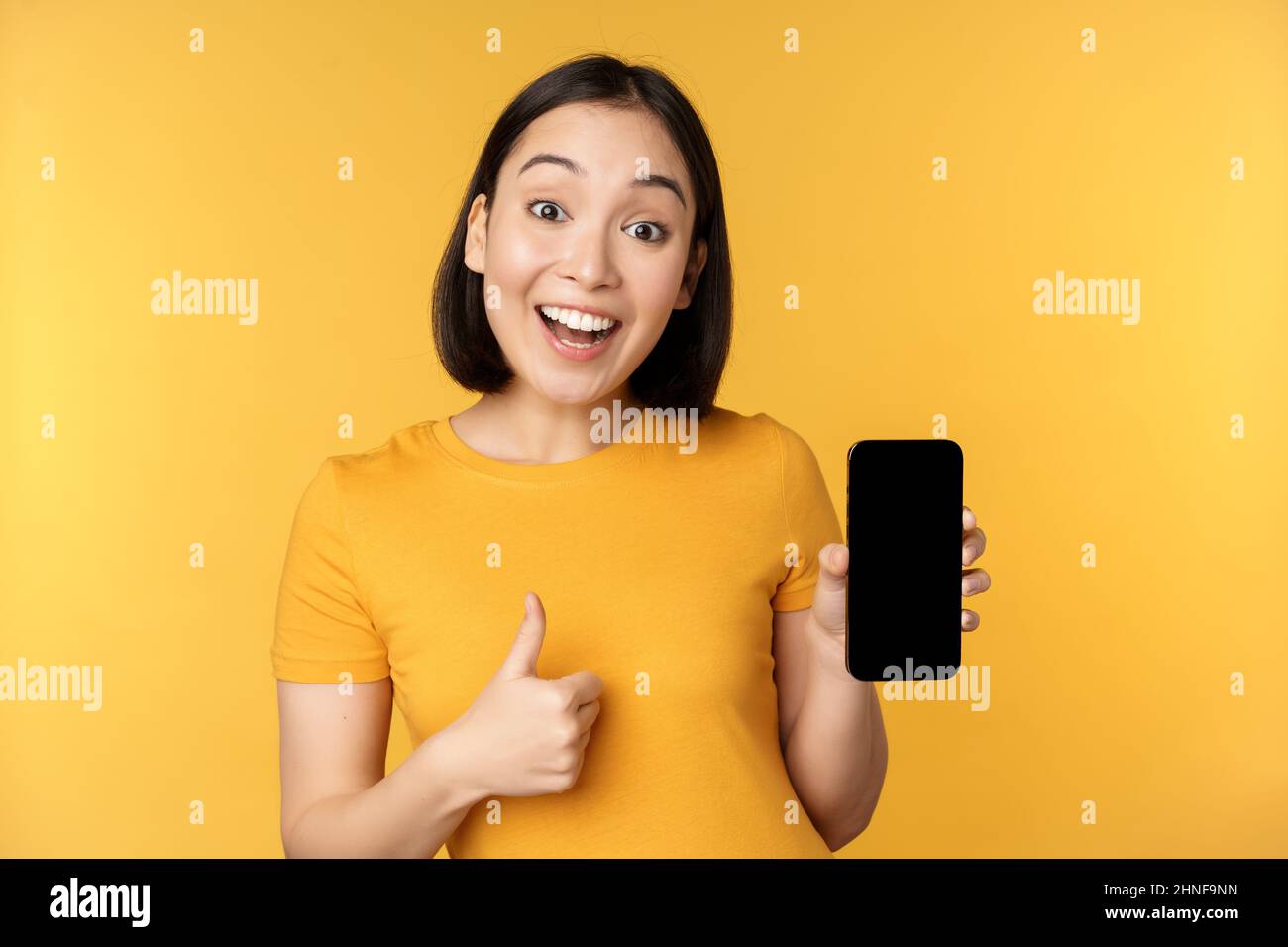 Excited asian woman showing mobile phone screen, thumbs up, like smth ...