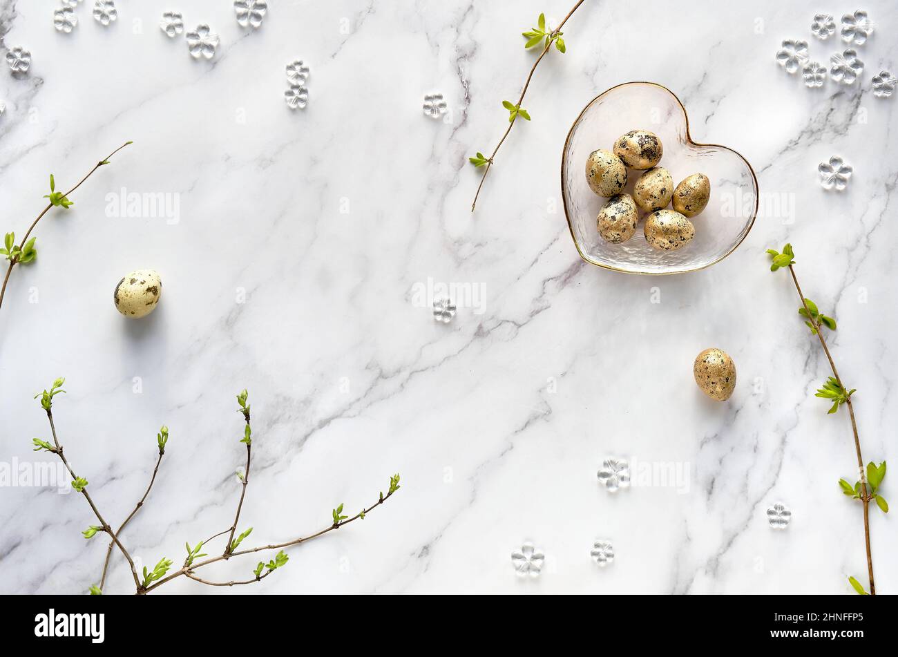 Golden quail eggs in glass heart shaped bowl. Twigs with young leaves ...