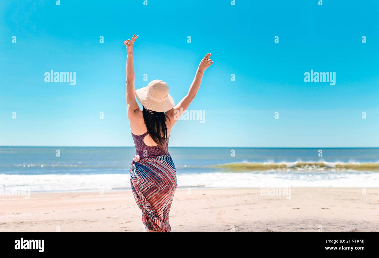 Woman with hat from back on the beach, young woman raising her hands on ...