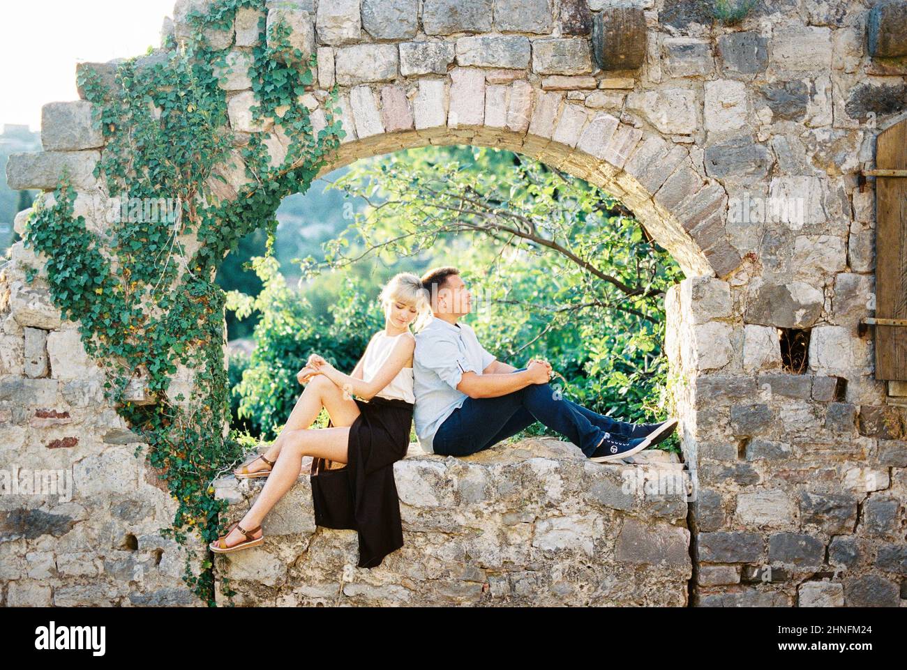Man and woman sit back to back in stone arch on castle ruins Stock ...