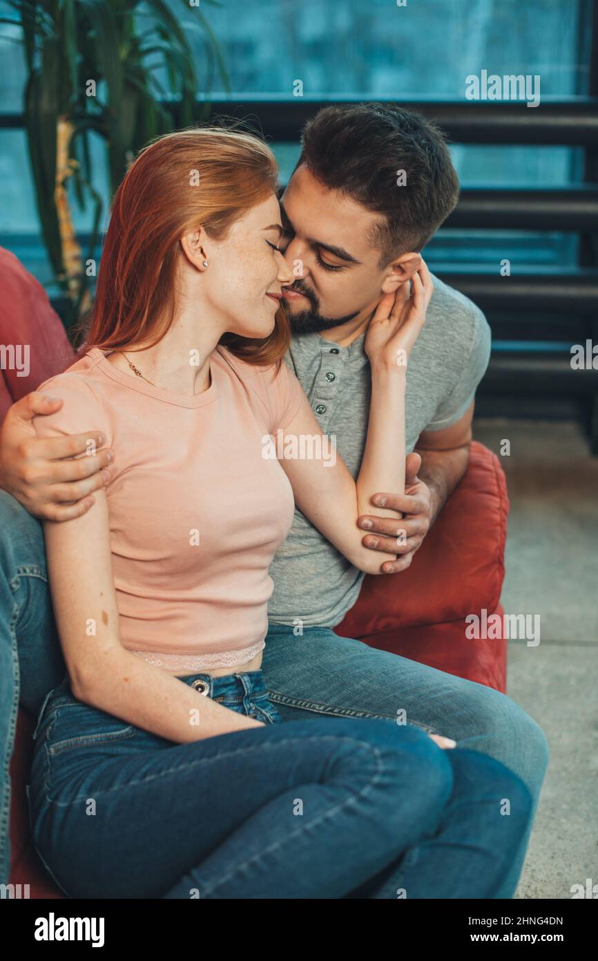 Portrait of romantic couple cuddling and kissing sitting on the sofa in ...