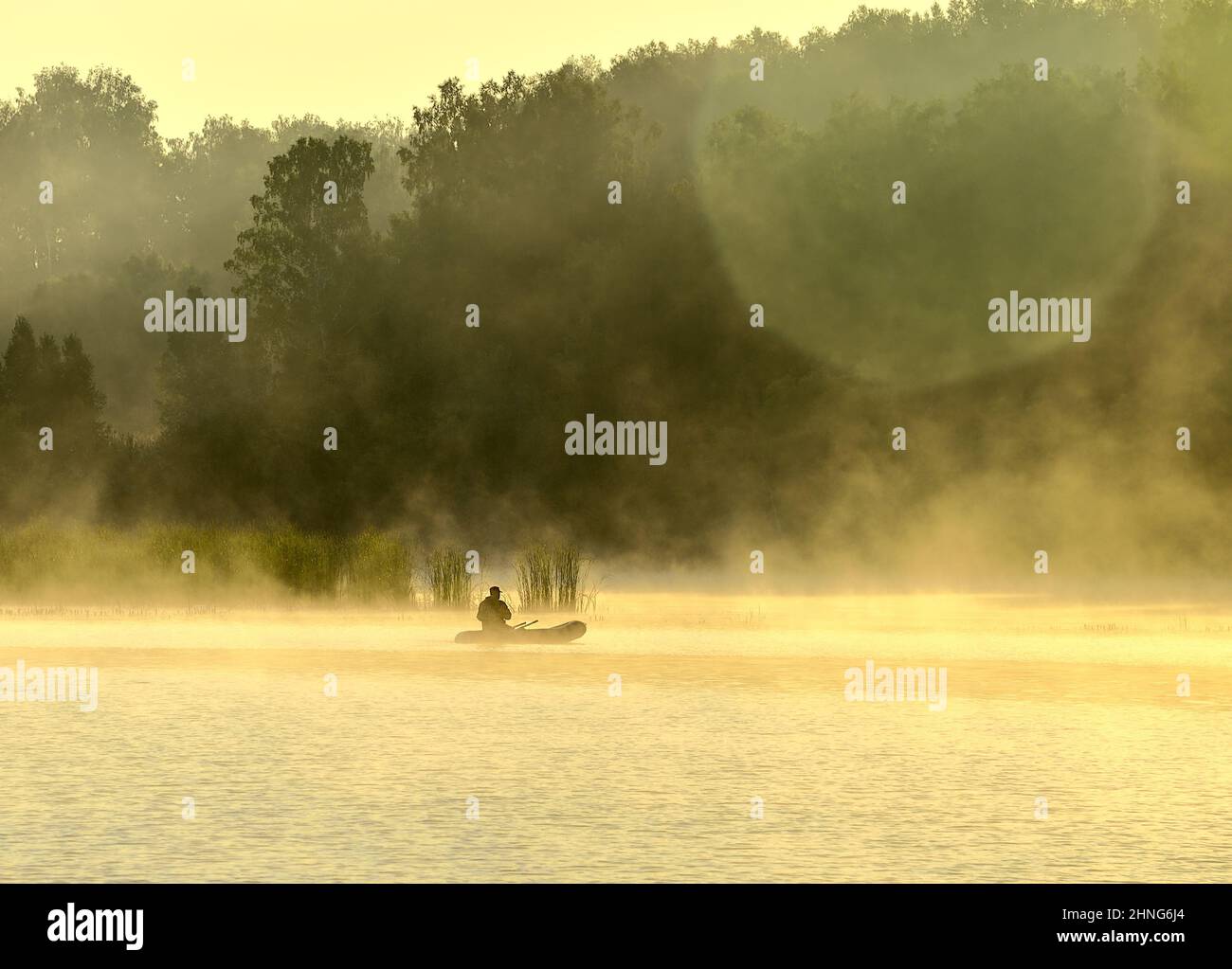 Morning on the shore of a forest lake, a fisherman on an inflatable ...