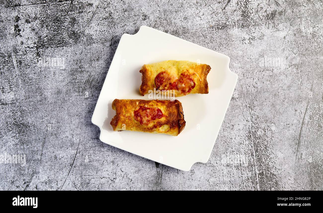 Toasted hot dog wraps on a white square plate on a dark background. Top ...