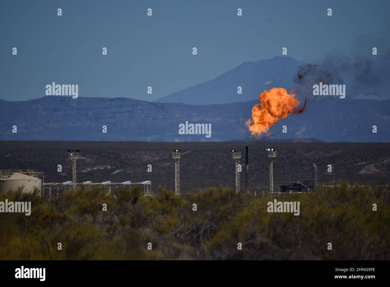 Of natural gas flare at an oil and gas filed against mountains and blue ...