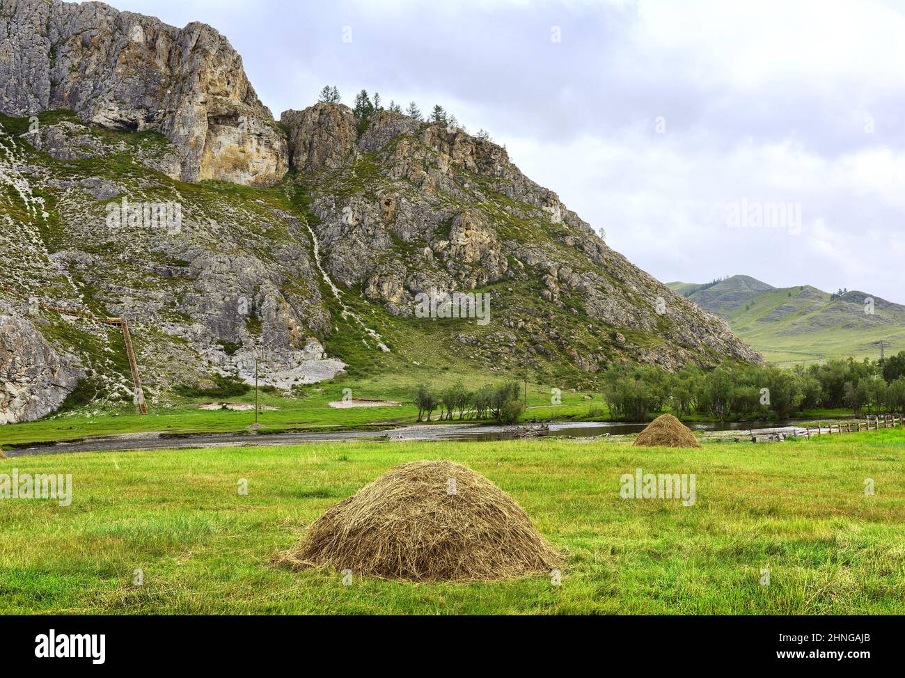 A haystack on a pasture against a high cliff under a blue cloudy sky ...
