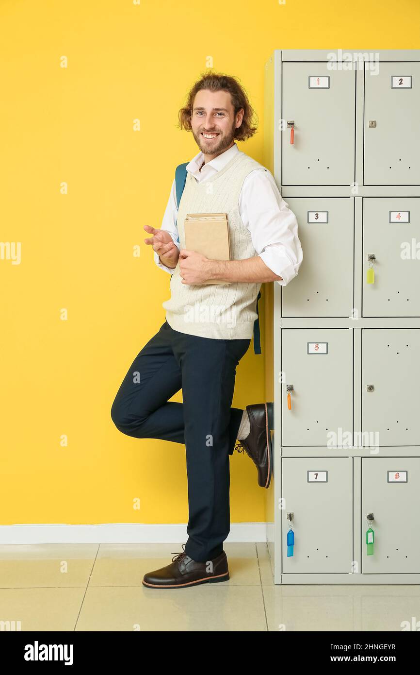 Male student with books near locker on yellow background Stock Photo ...