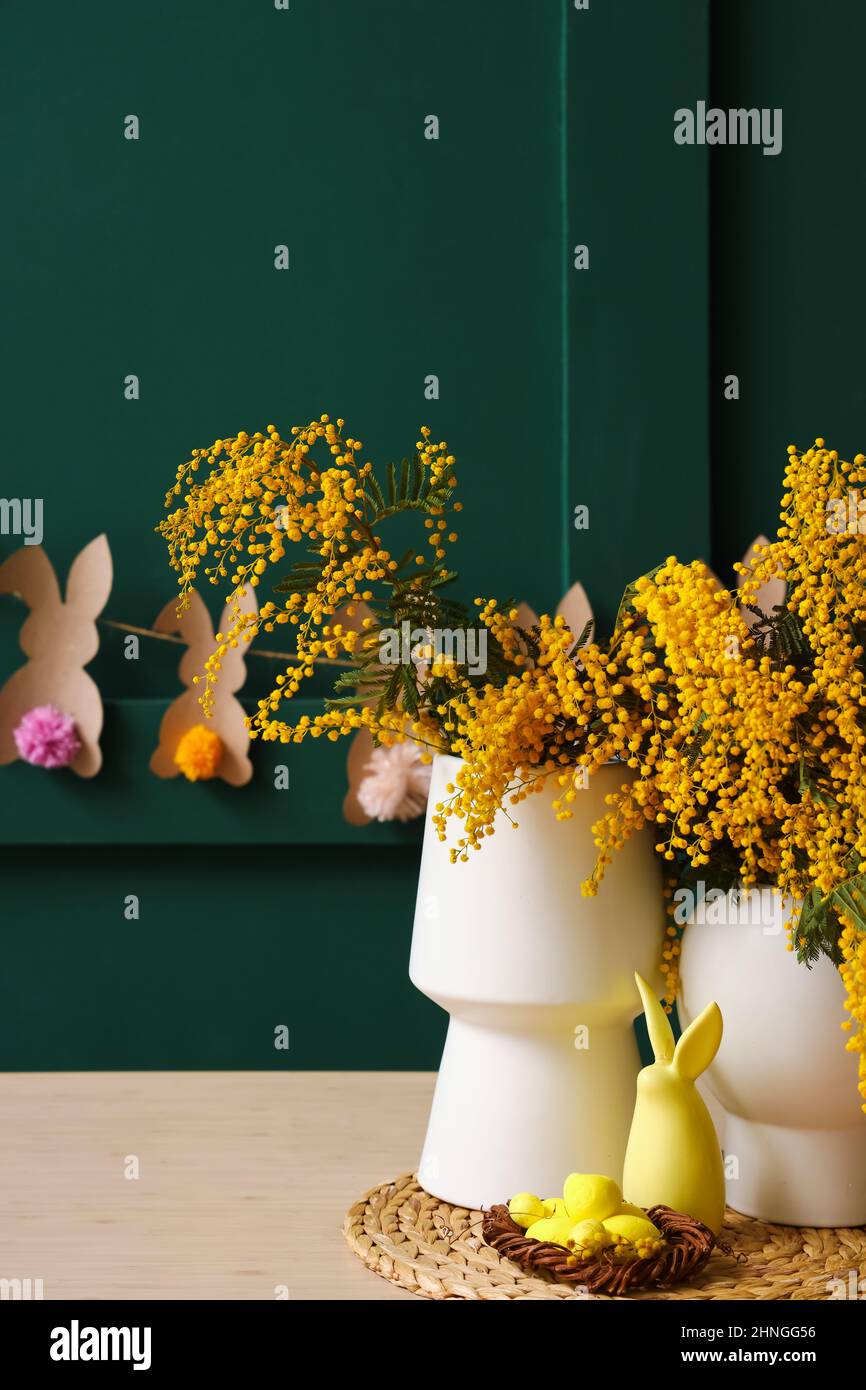Vases with mimosa flowers, Easter eggs and decor on dining table near ...