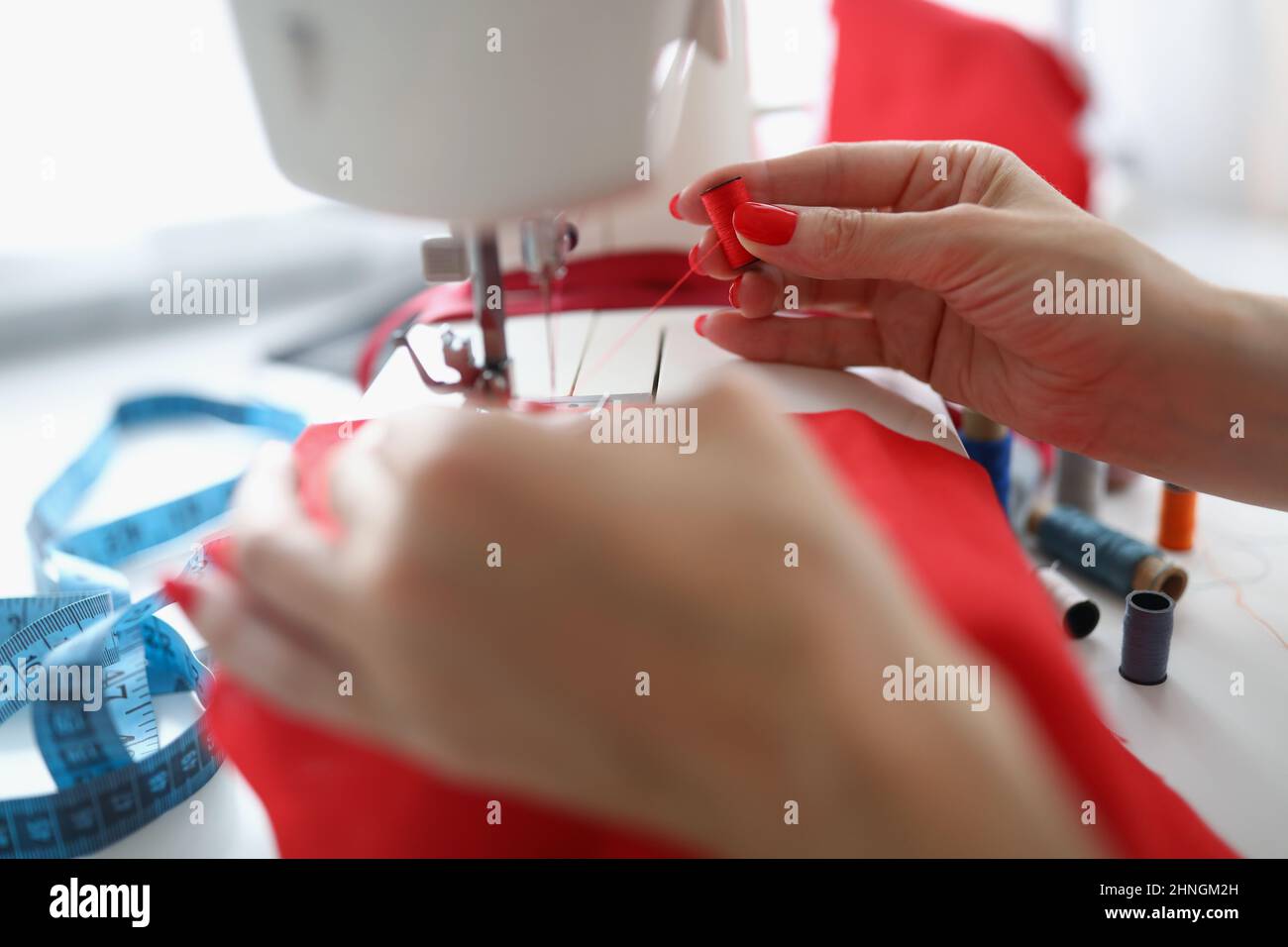 Female hands thread red thread into a sewing machine Stock Photo - Alamy