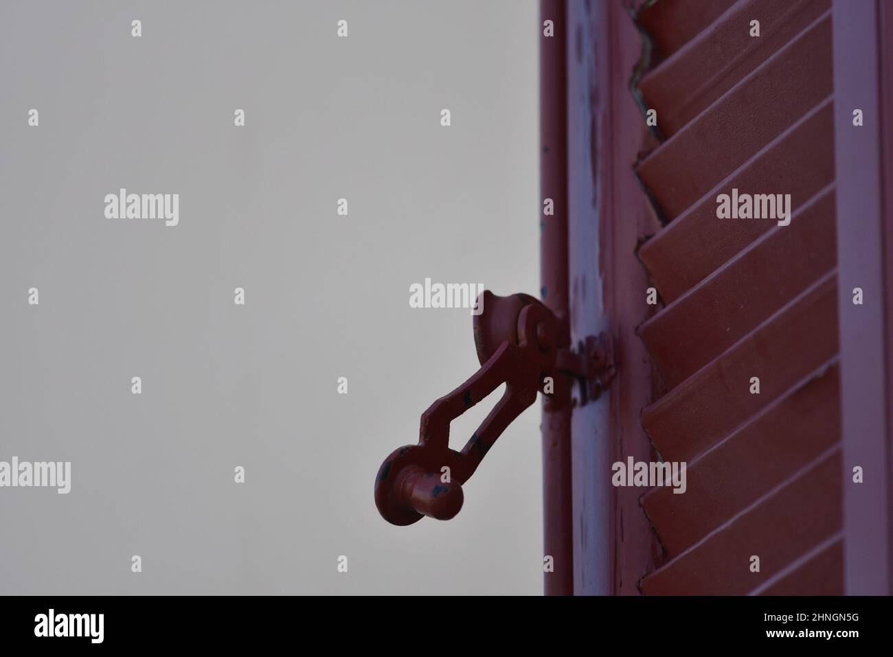 Traditional red wooden window shutter with a metal latch against a ...