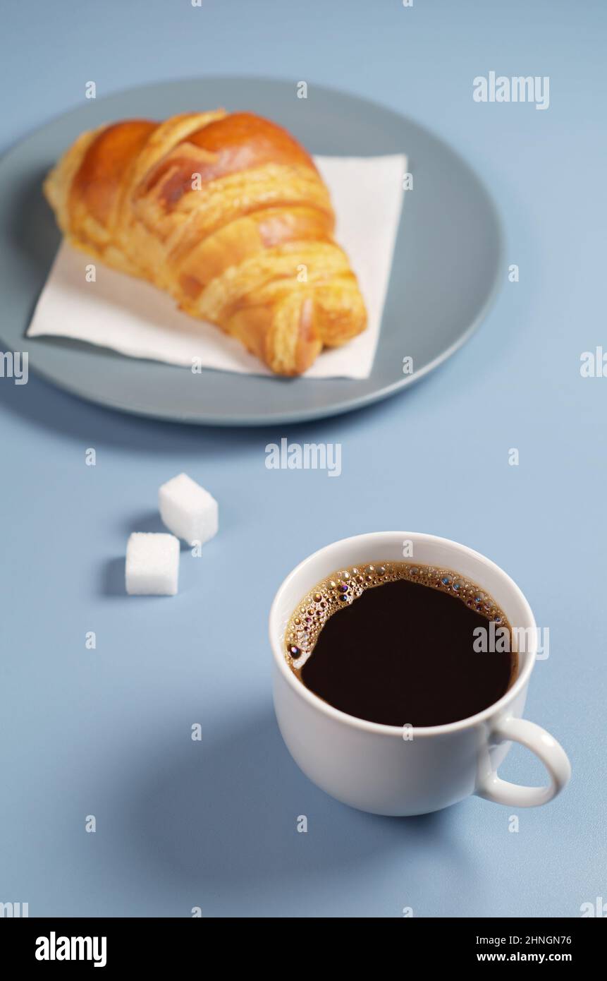 Cup of coffee and croissant in gray plate on blue table. Theme of ...
