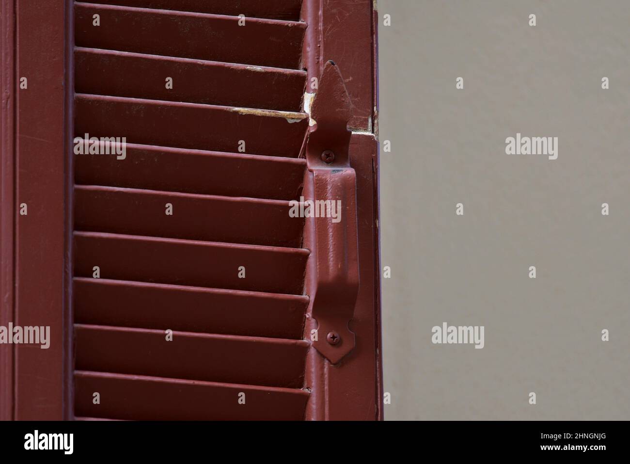 Traditional red wooden window shutter with a metal latch against a ...