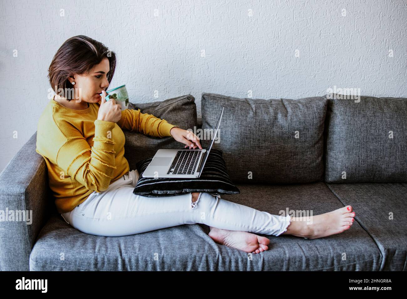 Hispanic woman sitting on sofa at home holding laptop computer for a ...