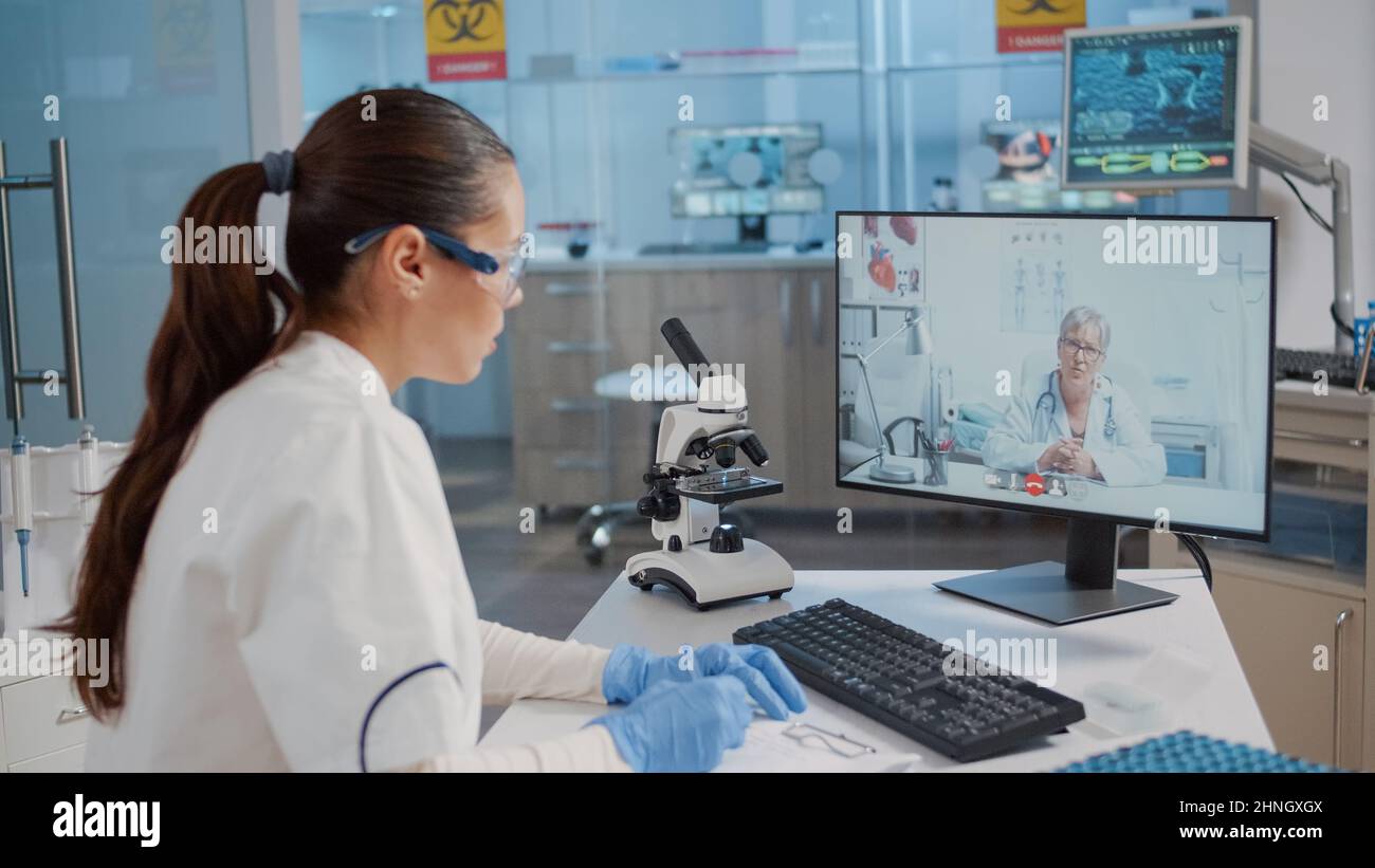 Chemist using online video call on computer in laboratory to work with ...