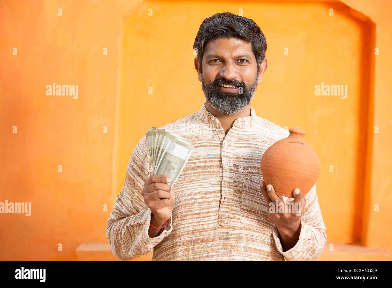 Portrait of happy man holding indian rupee notes and clay money box or ...