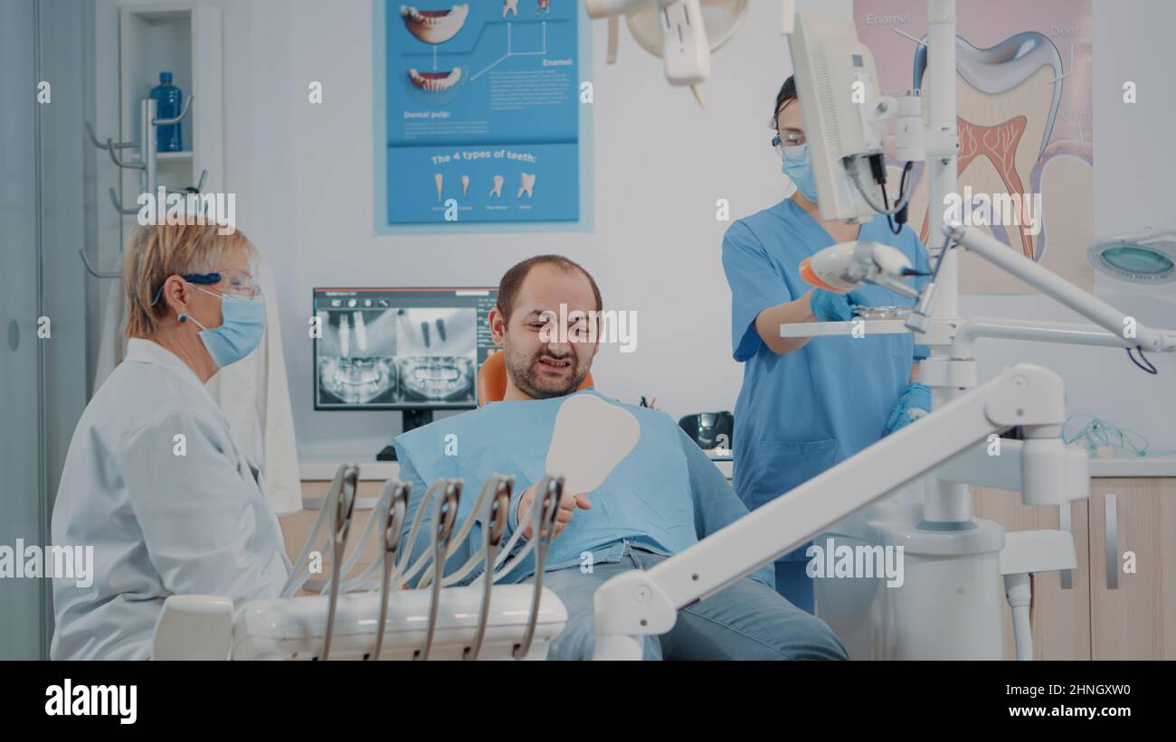 Patient holding mirror to see teeth alignment after dental procedure ...