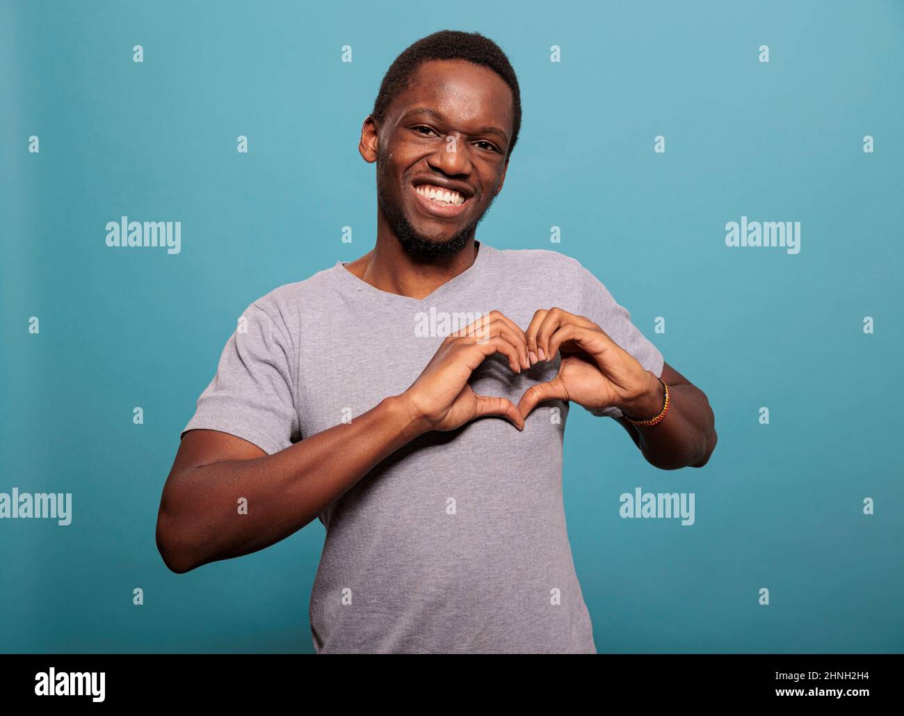 Young adult doing heart shaped sign with hands in studio, expressing ...