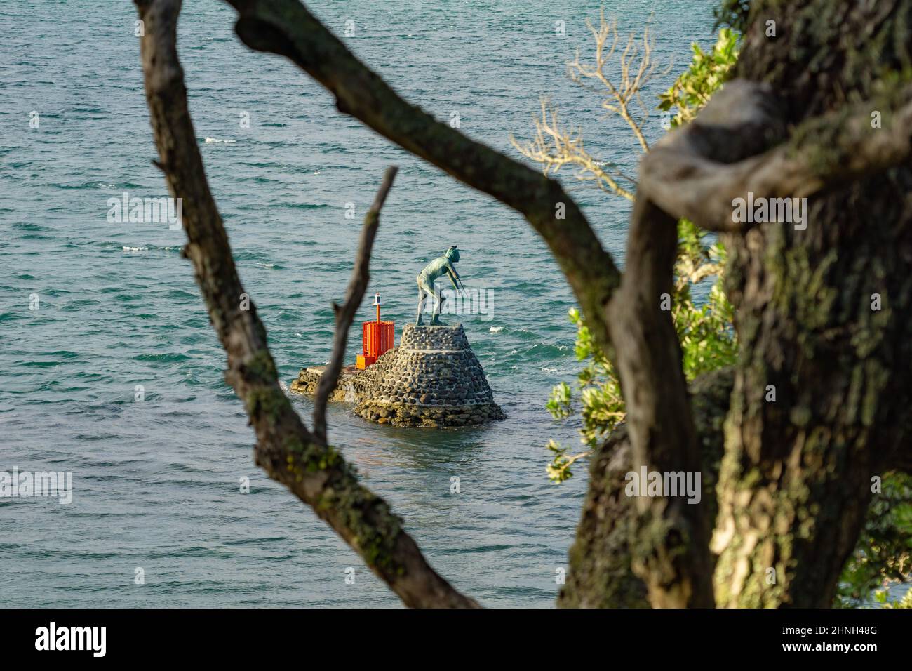 Tangaroa, mythical God of the Seas, statue framed by twisted branches ...