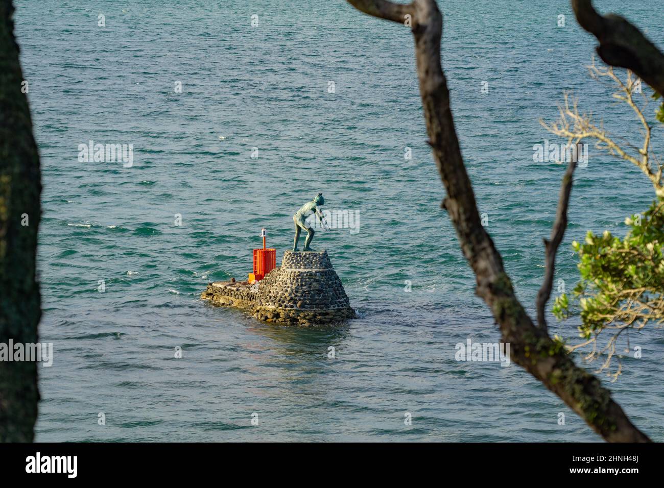 Tangaroa, mythical God of the Seas, statue framed by twisted branches of pohutukawa trees on ...