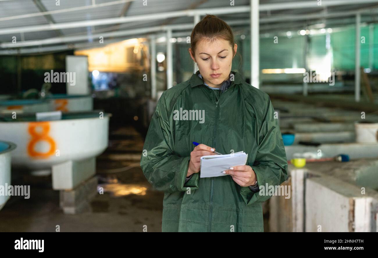 Female worker of trout farm watching fish and writing Stock Photo - Alamy