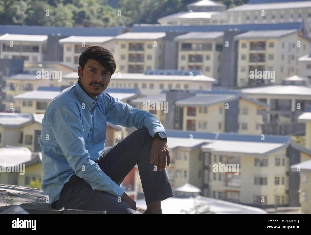 A young guy looking at camera sitting outside with buildings in ...