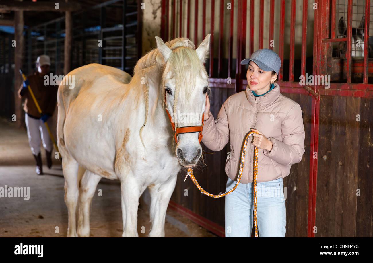 Young horsewoman caressing horse while leading to stall after riding ...