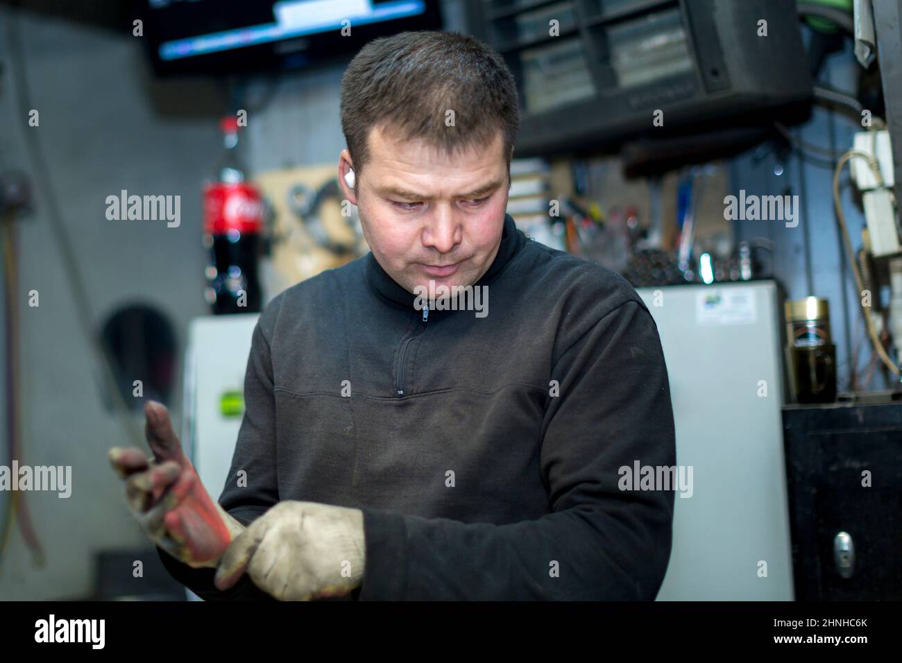 Close-up portrait of male worker at workplace wearing gloves and black ...