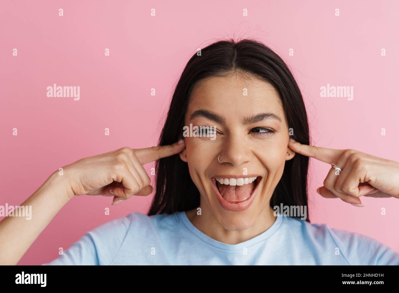 Young hispanic woman plugging her ears and laughing isolated over pink ...