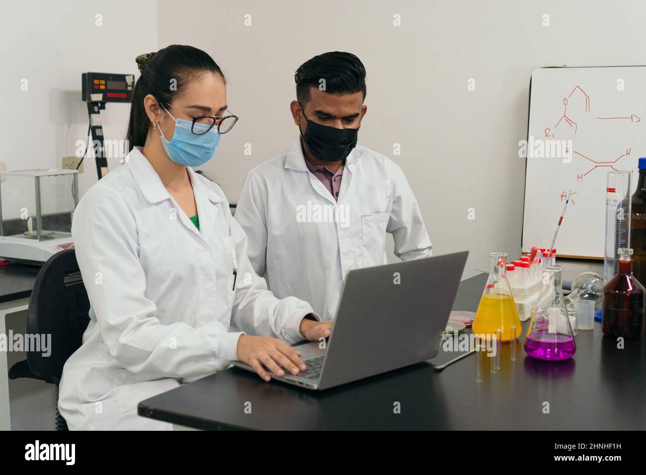 Two scientists working on a laptop in the lab. Wearing protective masks ...