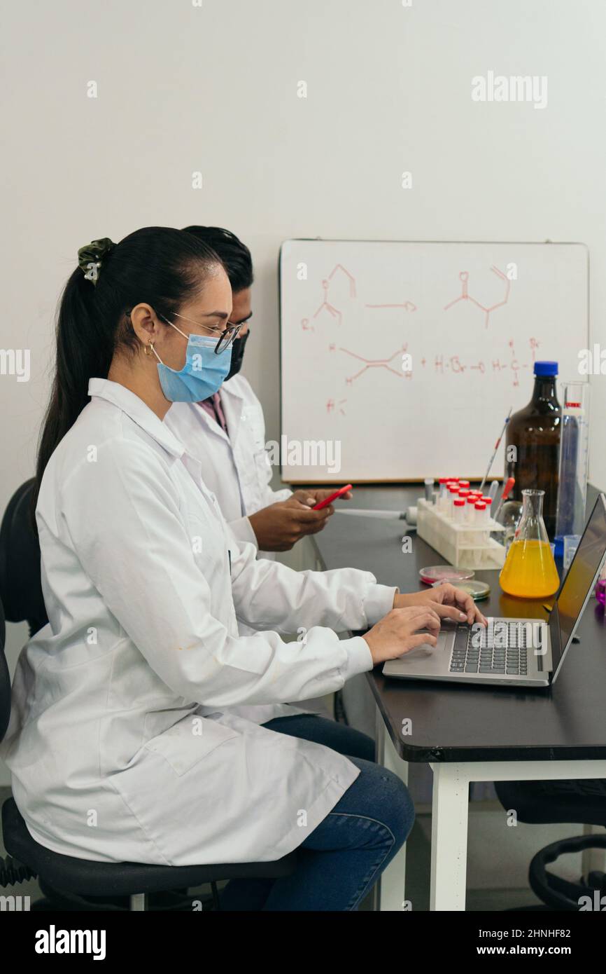 Two scientists working on a laptop in the lab. Wearing protective masks ...
