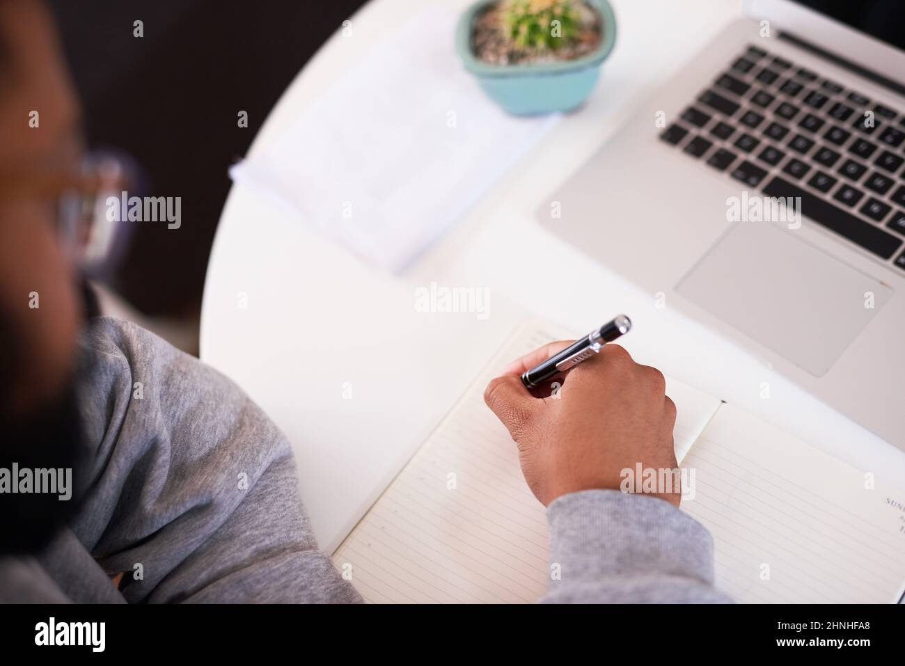 An over the shoulder shot of a young man writing at his desk Stock ...