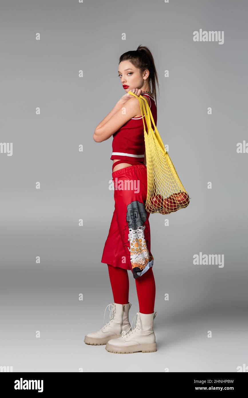 full length of trendy young model in red sportive outfit holding string ...