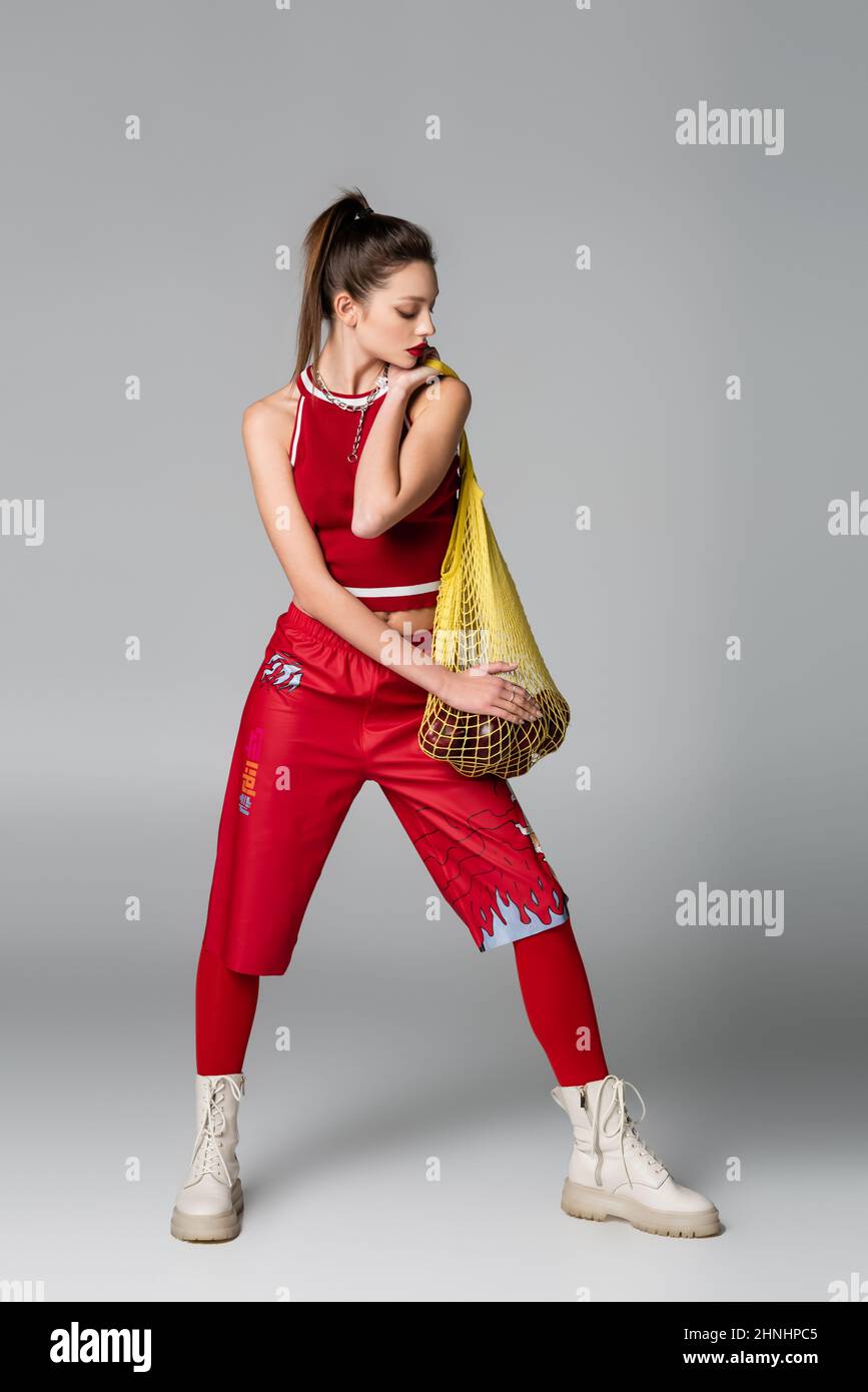 full length of trendy woman in red sportive outfit holding yellow ...