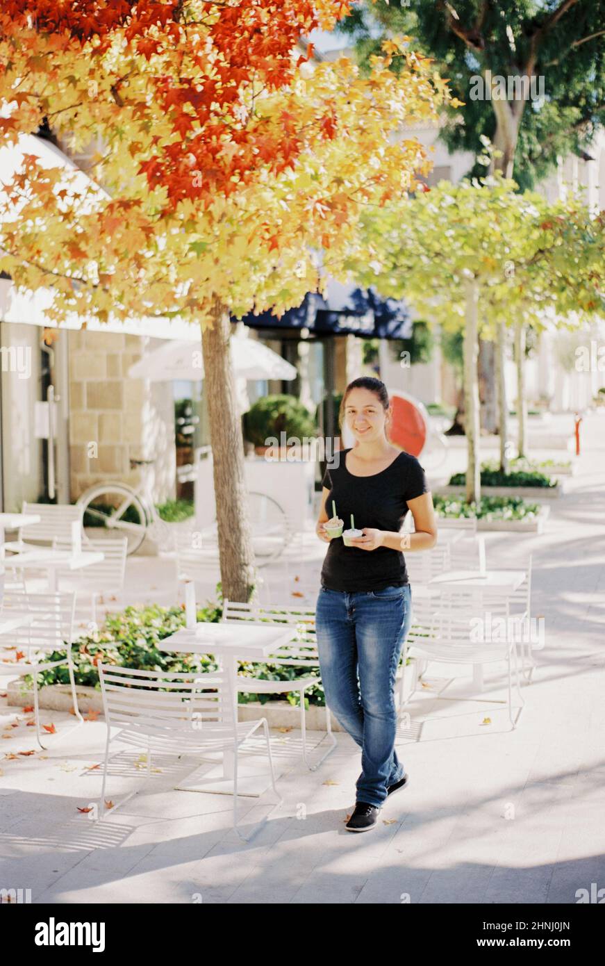 Smiling girl carries ice cream in cups to a table on the street under a ...
