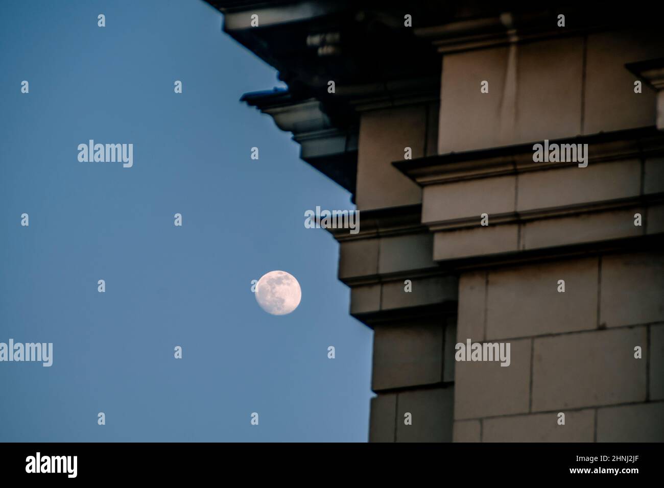 Full moon during the day on dusk next to a building roof. Beautiful ...