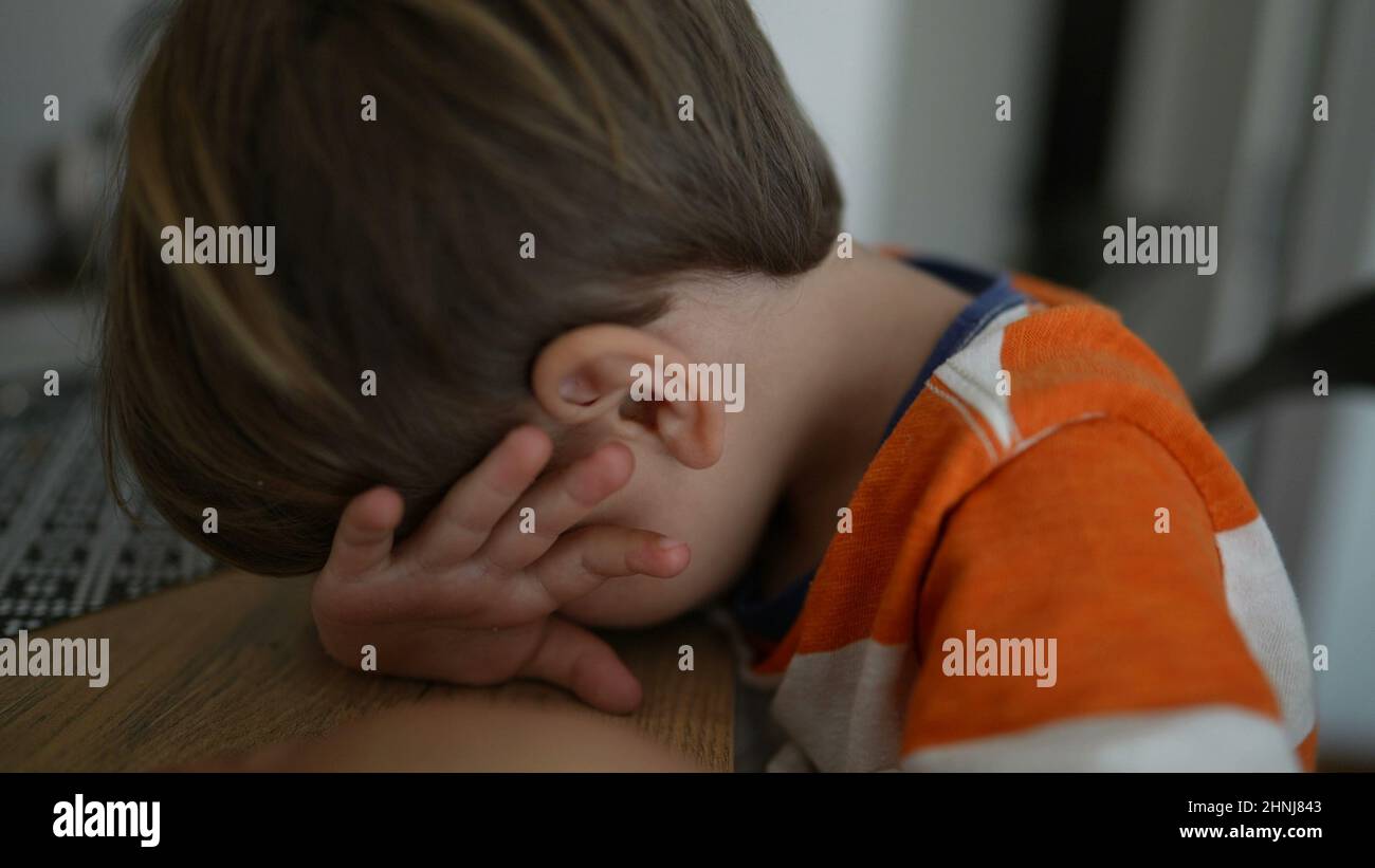 Shy Child covering face with hand little boy sitting at table feeling ...