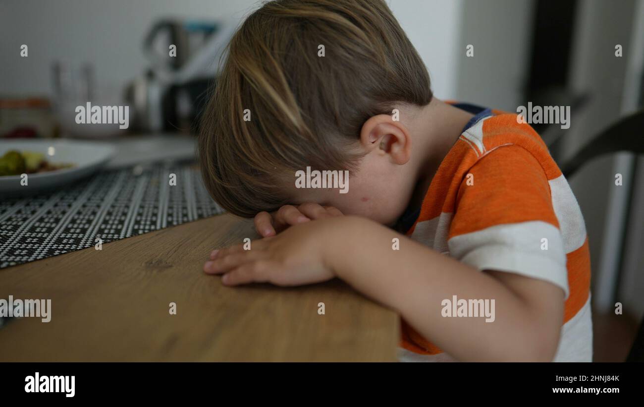 Shy Child covering face with hand little boy sitting at table feeling ...