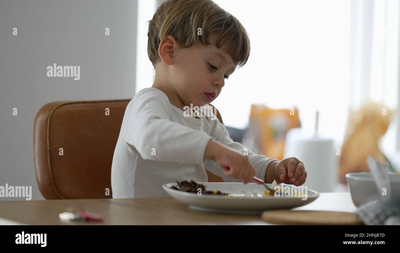 Toddler eating food by himself during lunch time baby using utensil ...