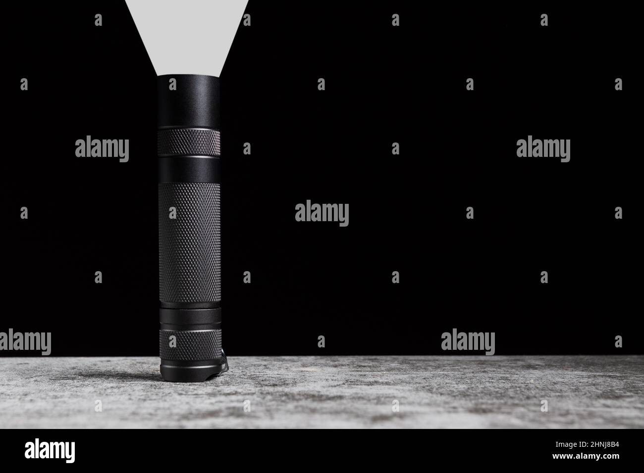 Flashlight stands on a table with beam of light upwards and copy space ...