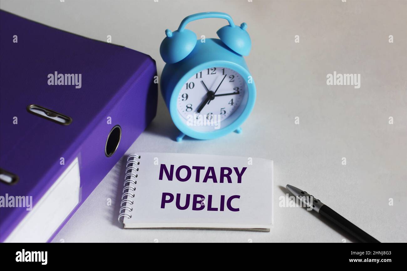 NOTARY PUBLIC written on a notebook next to a clock, a pen and a purple ...
