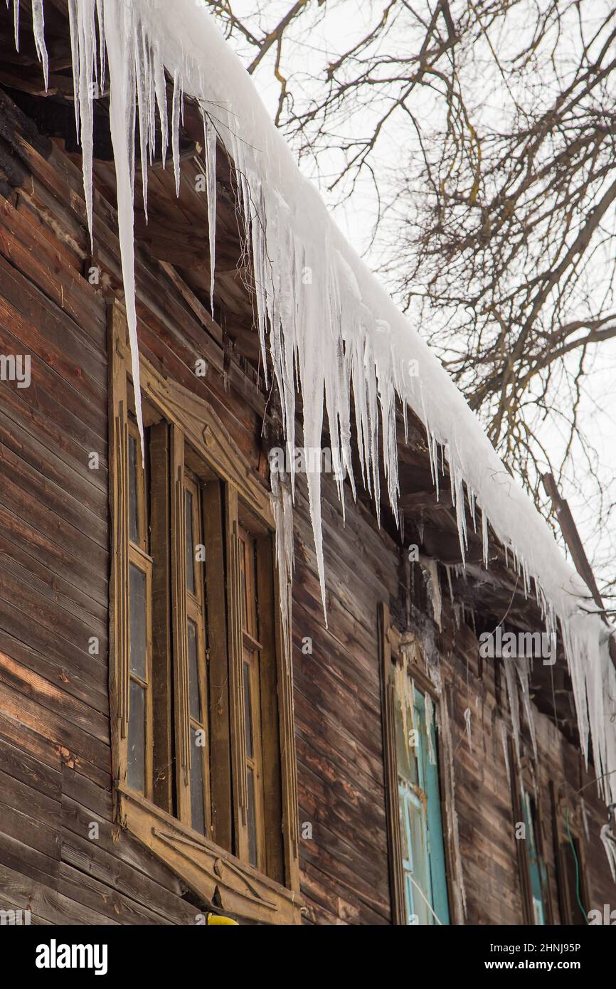 Crystal clear icicles hang on the edge of the roof. Against the ...