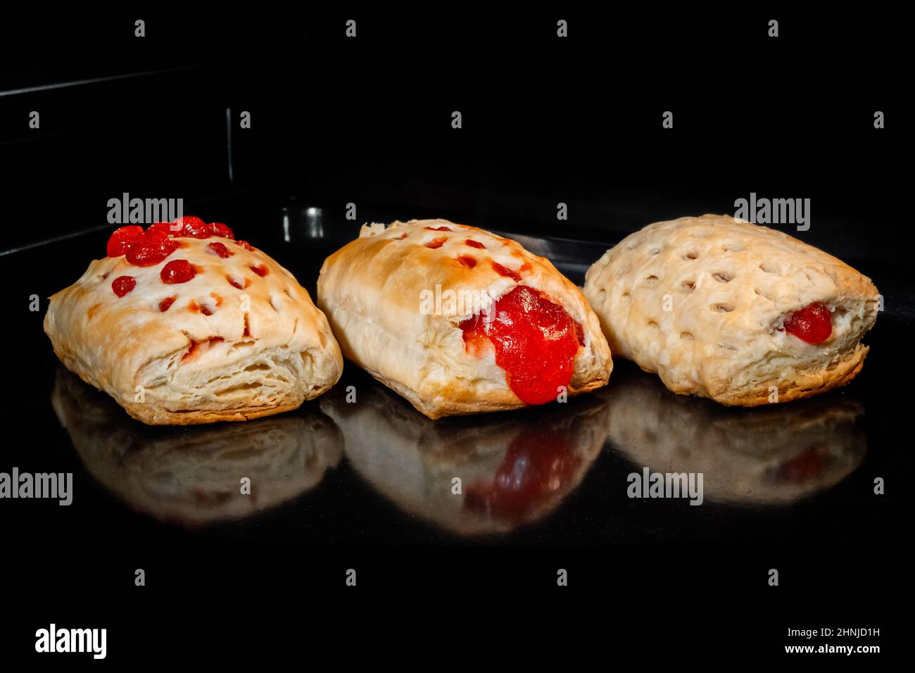 Three baked homemade buns with red strawberry jam on tray in electric ...